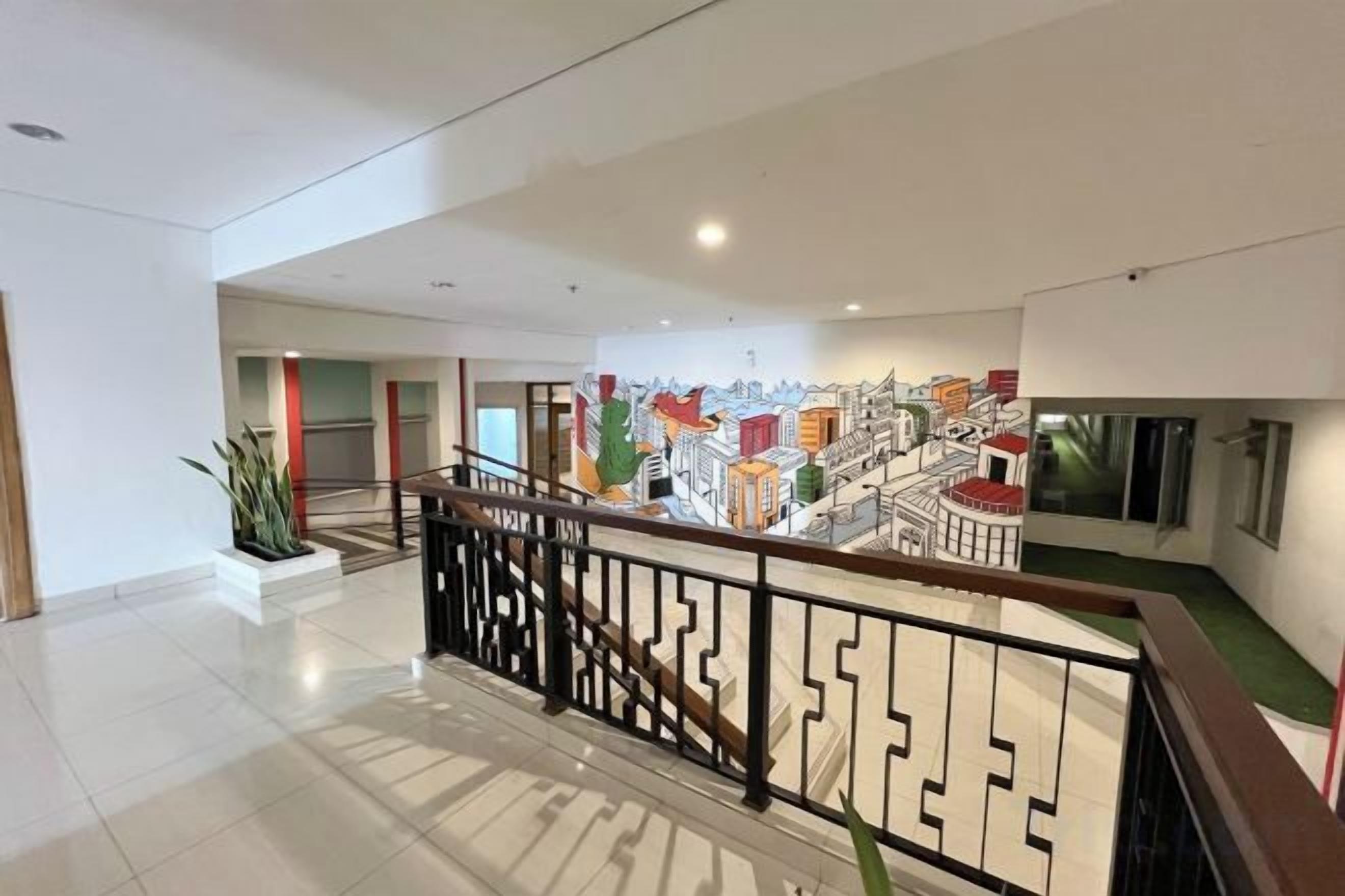 Um hall de hotel moderno com escada, um mural e uma planta.