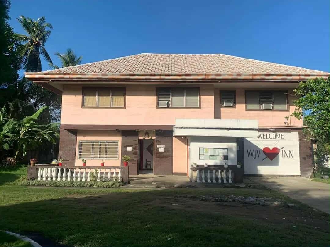 Um edifício de dois andares com telhado em telhas, um letreiro com a palavra 'Welcome' e um símbolo de coração indicando um hotel.