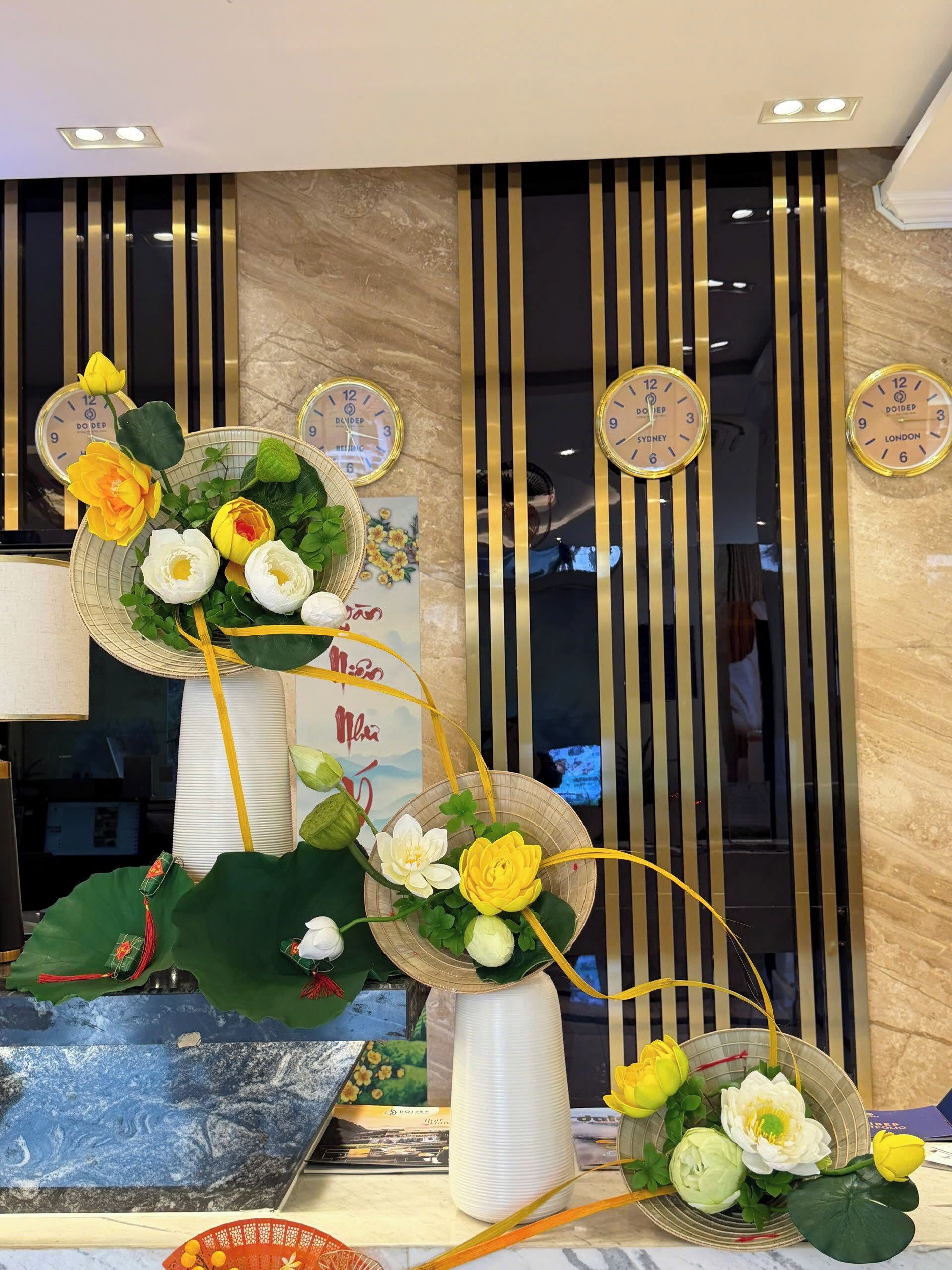 Uma área de recepção com design moderno, destacando um balcão de atendimento, arranjos florais decorativos e relógios exibindo diferentes fusos horários.