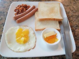 Prato de café da manhã com ovos, torradas, linguiça e feijão.