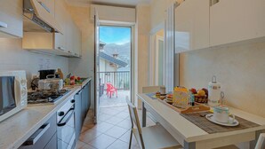 Cozinha pequena com vista para uma varanda, área de jantar com mesa posta para dois e uma geladeira compacta.