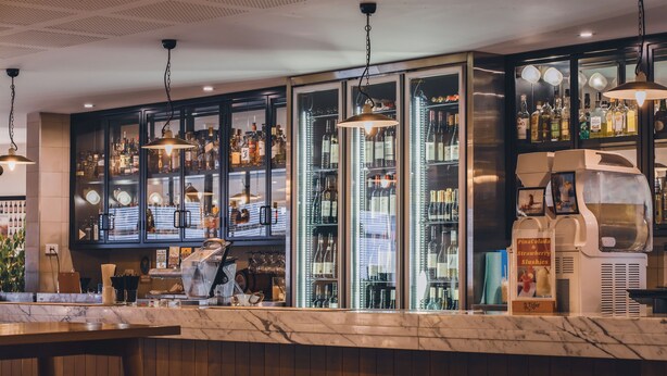 Uma área de bar com bancada de mármore, painéis de madeira e diversas garrafas de bebidas alcoólicas em vitrines.