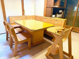 Uma sala de jantar com uma grande mesa retangular, seis cadeiras de madeira e um armário com portas de vidro ao fundo.