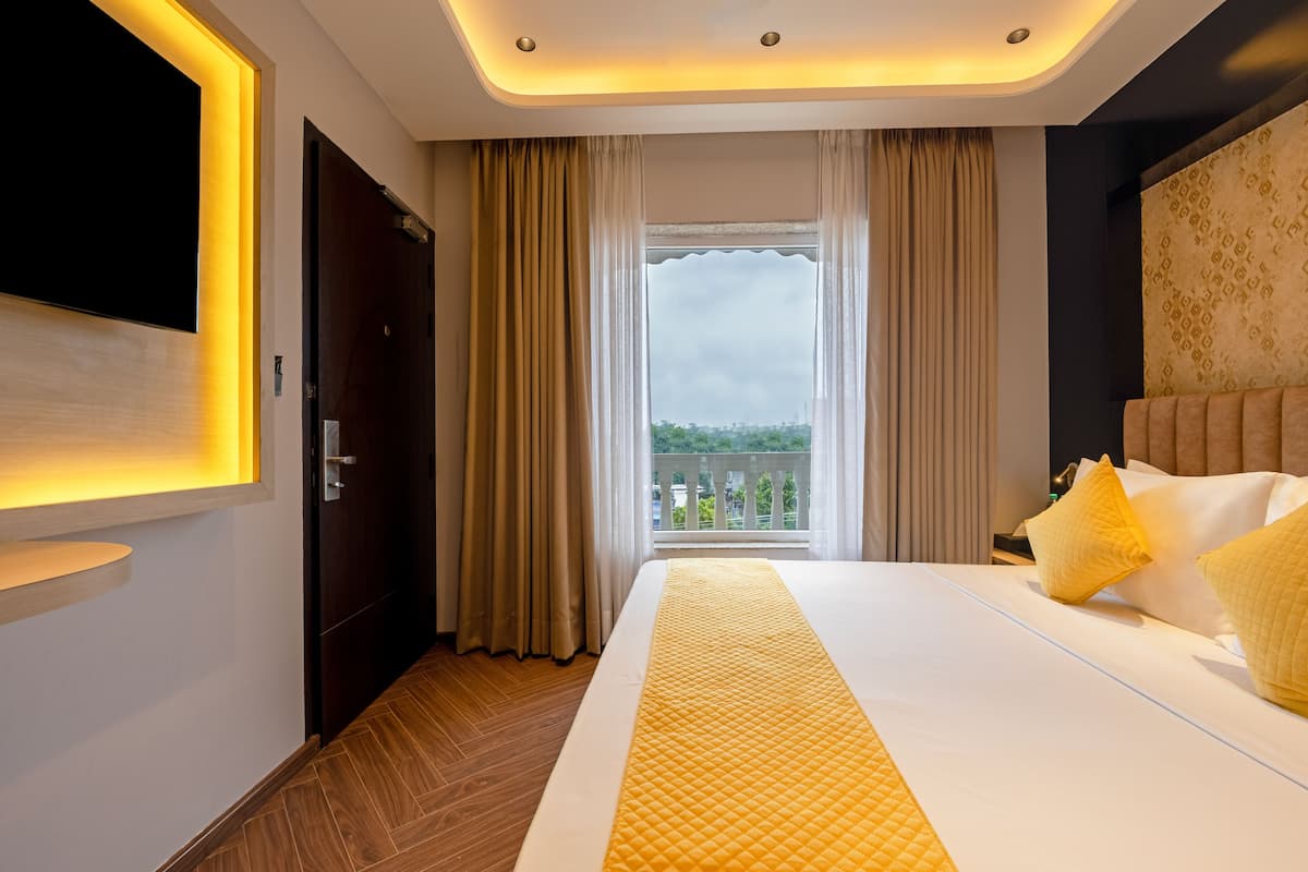 Quarto de hotel com uma cama grande, televisão na parede, janela com cortinas e vista para a varanda.