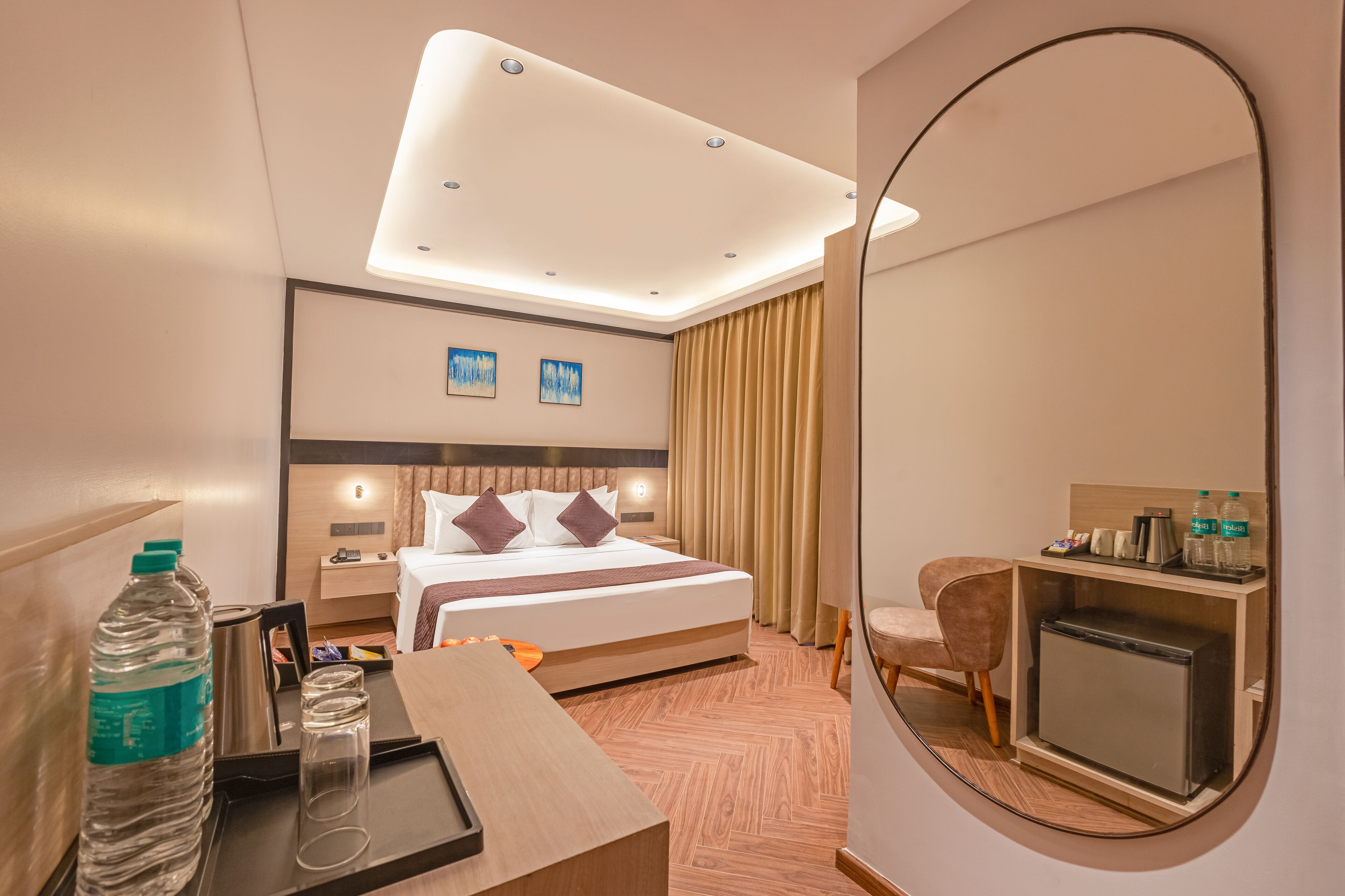 Quarto de hotel moderno com uma cama bem arrumada, uma escrivaninha com frigorífico, um espelho e um minibar.
