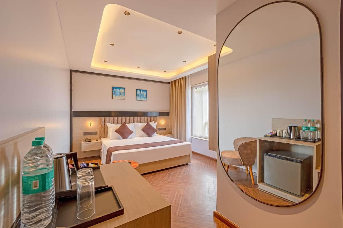 Quarto de hotel moderno com cama, mesa de cabeceira e uma pequena cozinha.