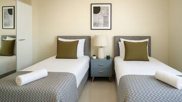 Quarto de hotel com duas camas, uma mesinha de cabeceira, uma luminária e uma obra de arte abstrata emoldurada na parede.