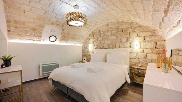 Quarto com teto de pedra, cama com roupa branca, mesa de cabeceira, uma pequena planta e um radiador.