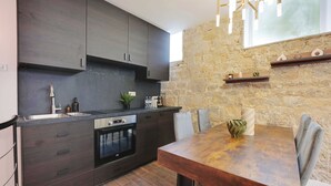 Uma cozinha moderna com armários escuros, forno embutido e área de jantar com mesa e cadeiras de madeira.