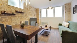 Uma sala de estar moderna com parede de pedra, mesa de jantar de madeira, sofá verde e uma grande janela que proporciona luz natural.