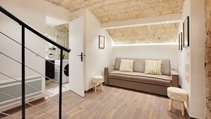 Uma sala de estar moderna com teto de pedra, um sofá com almofadas, um pequeno banquinho e um guarda-corpo de vidro.