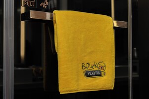 Uma toalha amarela pendurada em um suporte de metal para toalhas, com uma etiqueta bordada 'B.Dueck PLAYFUL'.