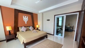 Quarto moderno com uma cama grande, duas luminárias de cabeceira, um painel decorativo na parede e vista para uma sala de jantar através de uma porta de vidro.