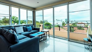 Uma sala de estar moderna com um sofá grande, uma mesinha e vista para uma área residencial através de amplas janelas.