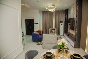 Uma sala de estar moderna com área de jantar, apresentando um conjunto de sofá, uma TV fixada na parede e um vaso decorativo na mesa de jantar.