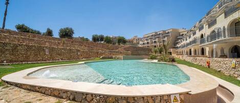 Piscina rodeada por paredes de pedra e um edifício com varandas.