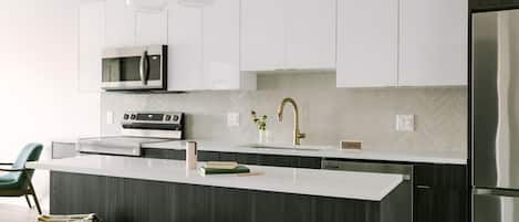 Uma cozinha moderna com armários brancos, uma ilha central com banquetas, micro-ondas, fogão e geladeira.