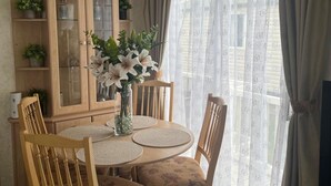 Uma área de refeições com uma mesa redonda, duas cadeiras, um vaso com flores brancas e um armário de madeira com portas de vidro.