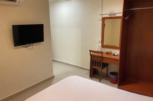 Quarto de hotel com cama, televisão na parede, secretária de madeira com cadeira, espelho e guarda-roupa.