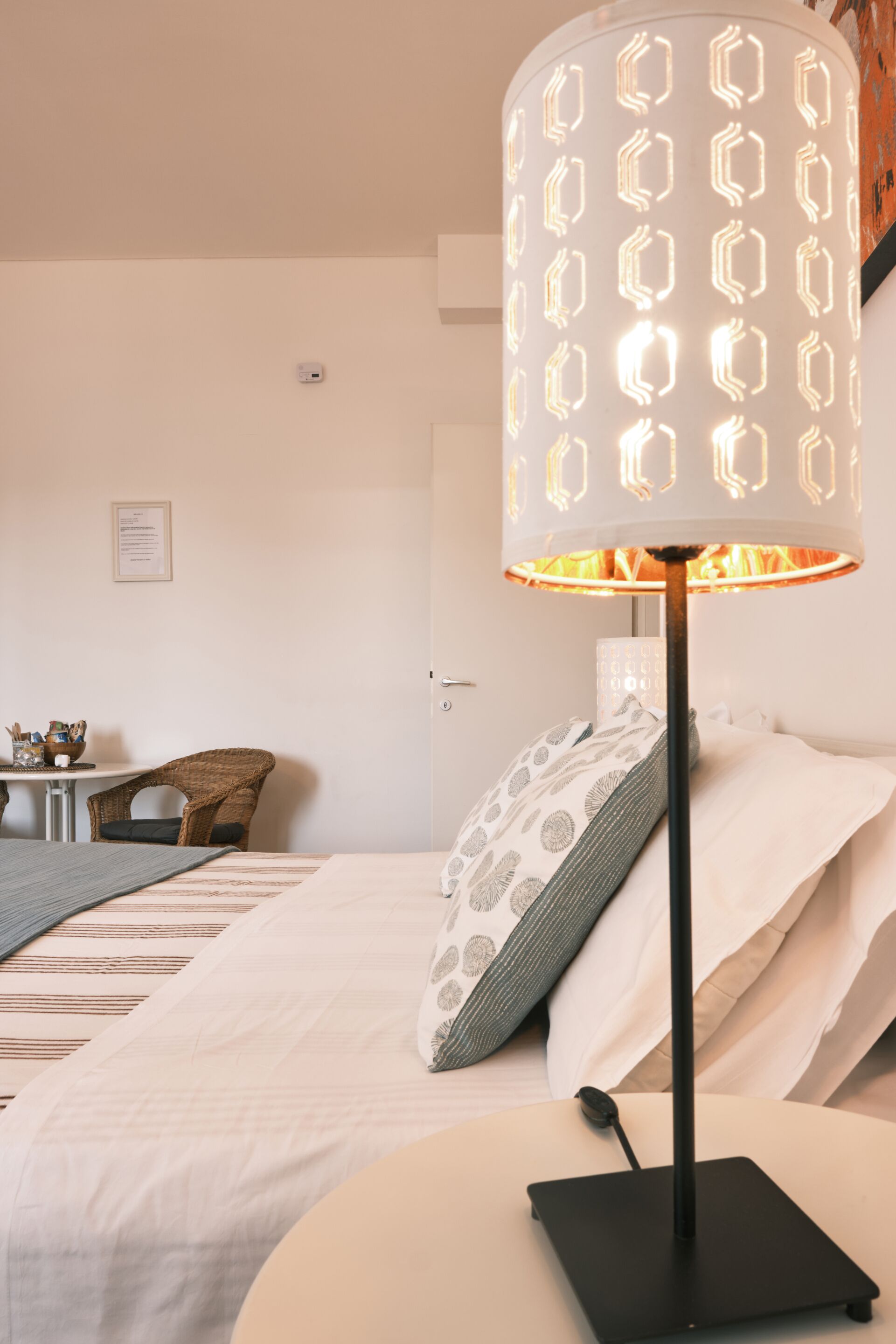 Quarto de hotel bem arrumado, com cama, mesa de cabeceira, abajur e uma cadeira.