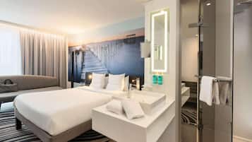 Quarto de hotel moderno com cama, banheiro com espelho e pia, e chuveiro.