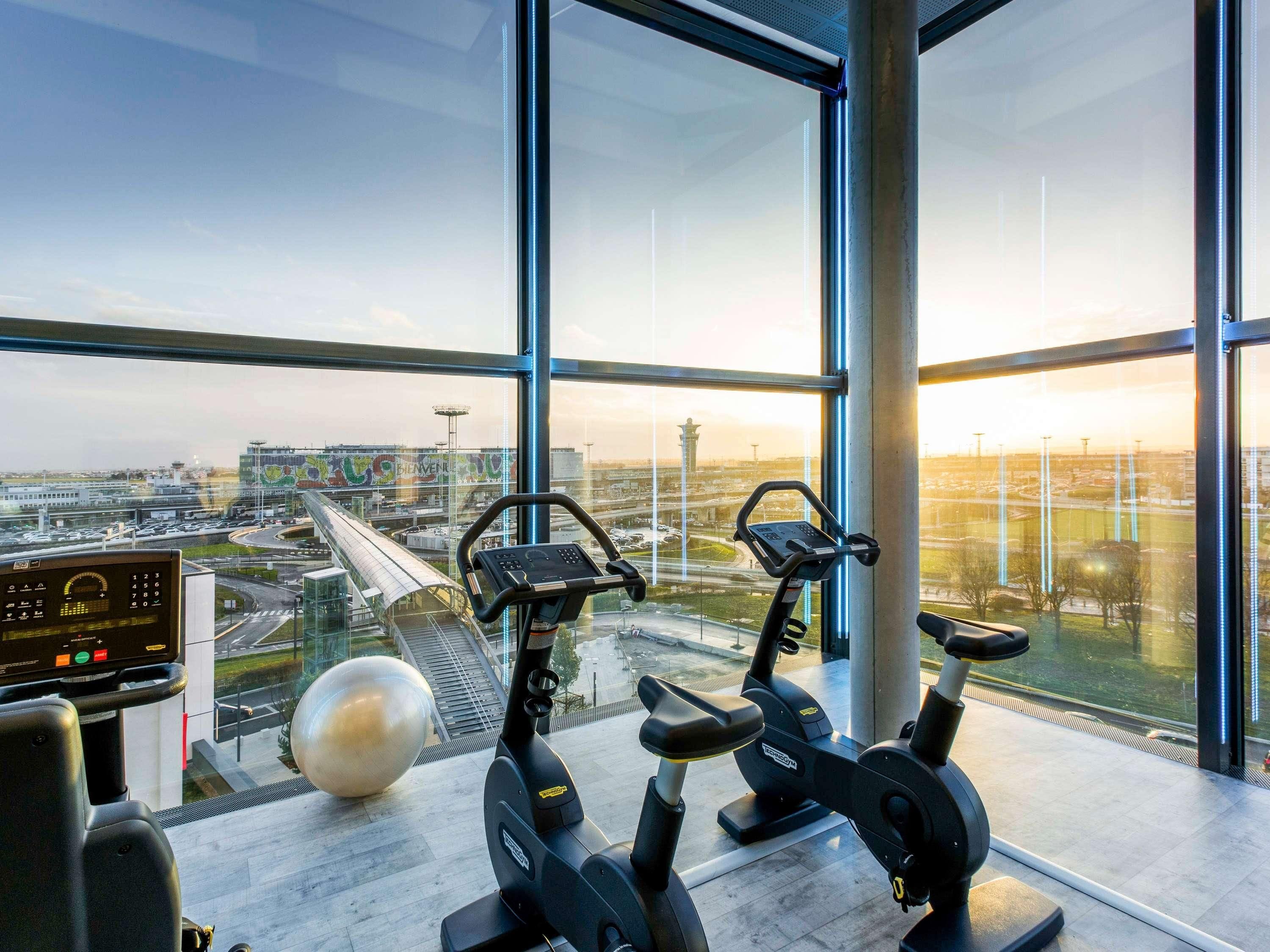 Uma academia com equipamentos de ginástica e uma grande janela com vista para um aeroporto.