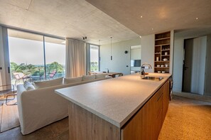 Cozinha moderna com uma ilha grande, sala de jantar com sofá e vista para o exterior.