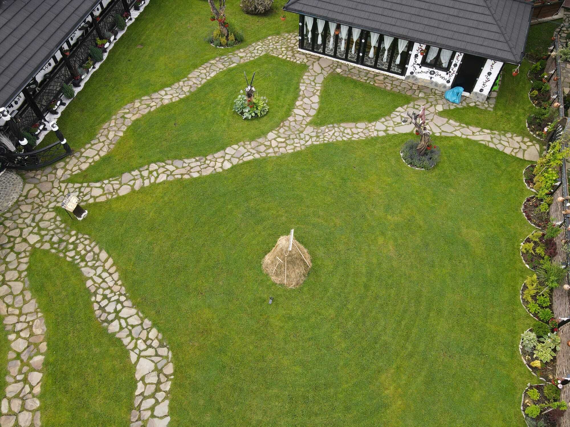 Um jardim ajardinado com um caminho de pedra, uma pequena árvore e um edifício com telhado preto.
