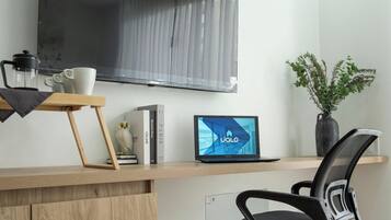 Um espaço de trabalho com um laptop, uma cafeteira, um vaso com plantas e uma estante de livros.