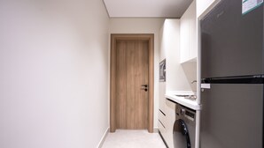 Um corredor estreito com uma porta de madeira, uma máquina de lavar e um refrigerador.