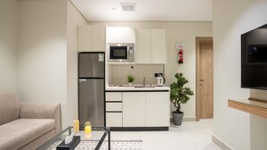 Uma cozinha moderna com armários brancos, micro-ondas, geladeira e um vaso de planta.