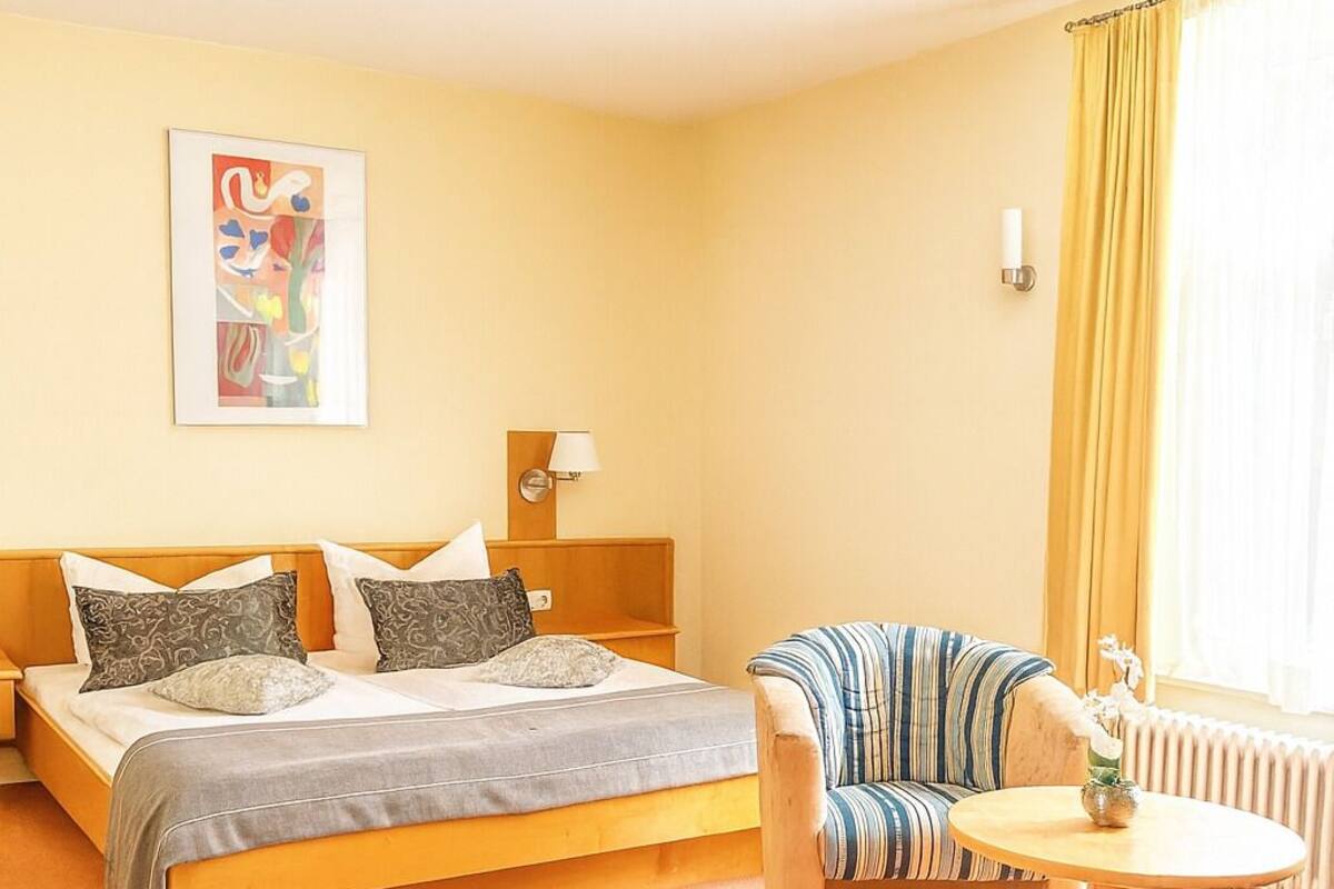 Quarto de hotel com uma cama, uma cadeira, uma mesa pequena, um abajur e um radiador.