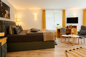 Quarto de hotel moderno com uma cama grande, uma escrivaninha, uma cadeira, uma televisão e uma janela com cortinas.