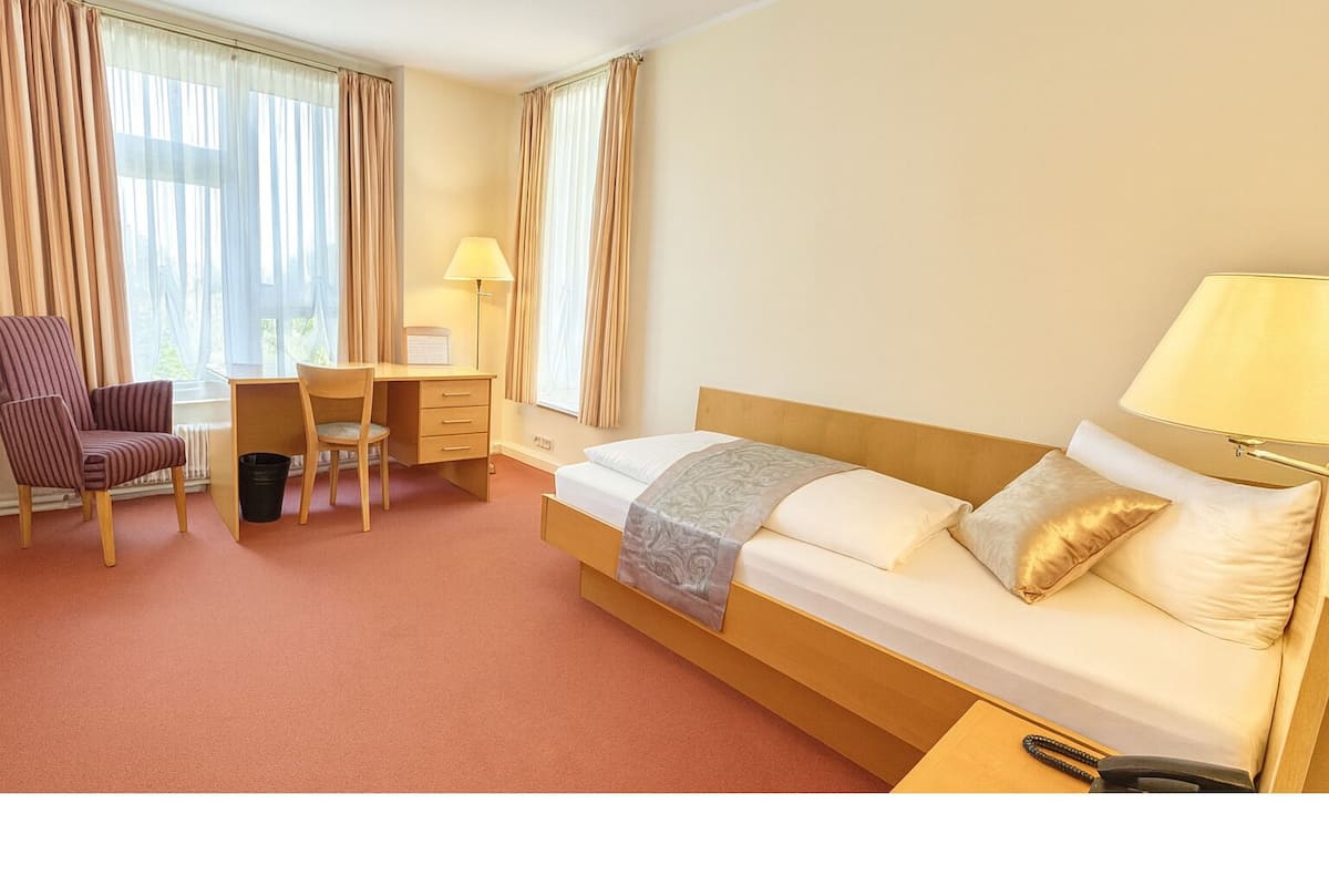 Quarto de hotel com cama, escrivaninha, cadeira e abajur.
