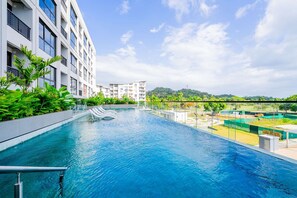 Um hotel moderno com piscina infinita no terraço, rodeado por vegetação exuberante e vista para colinas distantes.