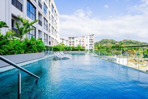 Um hotel moderno com piscina infinita no terraço, rodeado por vegetação exuberante e com vista para uma paisagem montanhosa.