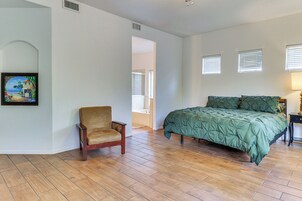 Quarto com piso de madeira, cama verde, cadeira marrom e um quadro na parede.