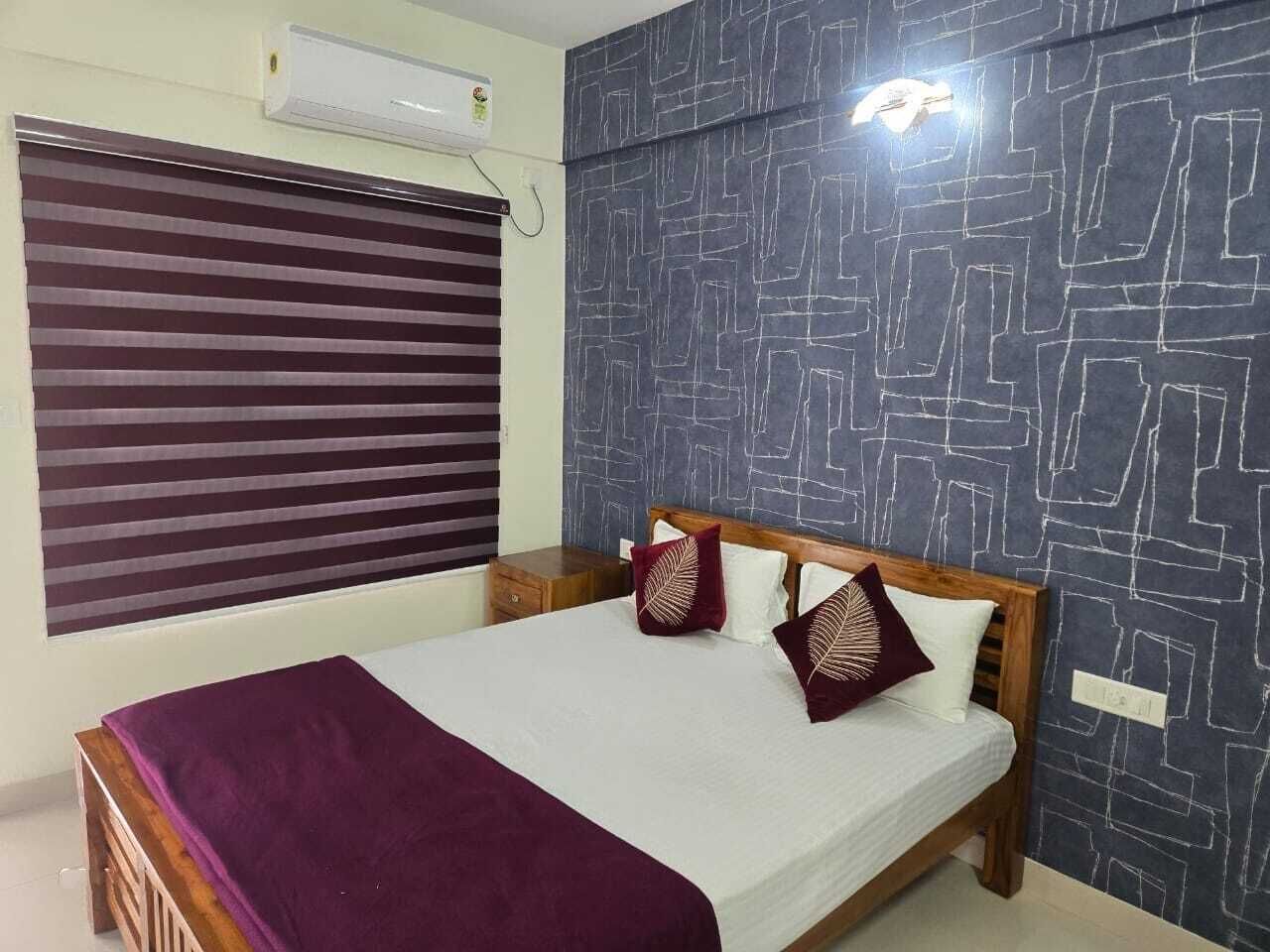 Quarto com cama, duas mesas de cabeceira, janela com persianas e parede com padrão geométrico.
