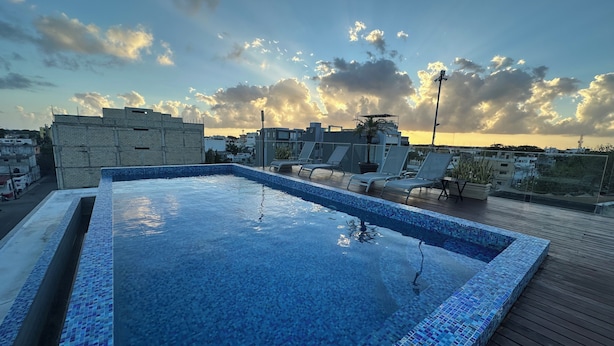 Uma piscina no terraço com borda azulejada, rodeada por cadeiras de sol e um deck de madeira.