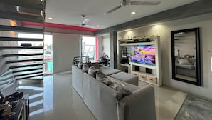 Uma sala moderna com um sofá cinza, uma televisão de tela plana, ventiladores de teto e uma escada com parede de destaque vermelha.