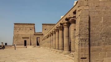 Uma entrada imponente com colunas altas e esculturas hieroglíficas, conduzindo a uma estrutura semelhante a um templo.
