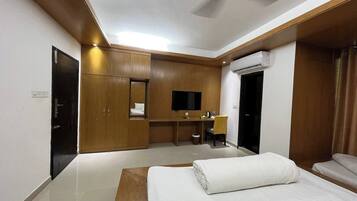 Quarto de hotel com cama, escrivaninha, cadeira, televisão e ar condicionado.