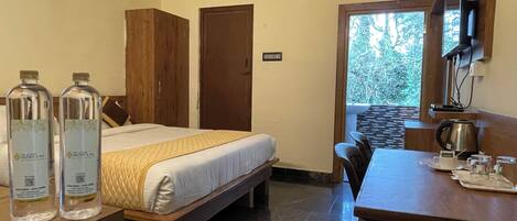 Quarto de hotel com cama, escrivaninha, cadeira, televisão e janela com vista para árvores.