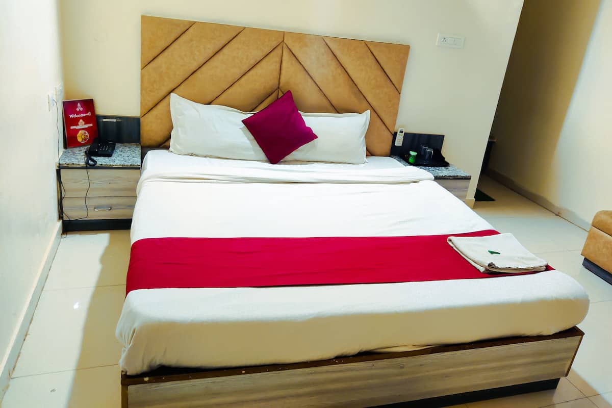 Cama bem arrumada com cabeceira de madeira, roupa de cama branca e manta vermelha.