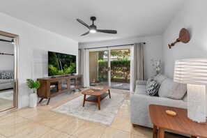 Uma sala de estar moderna com uma TV de tela plana, uma mesa de centro de madeira, um sofá cinza e um ventilador de teto.