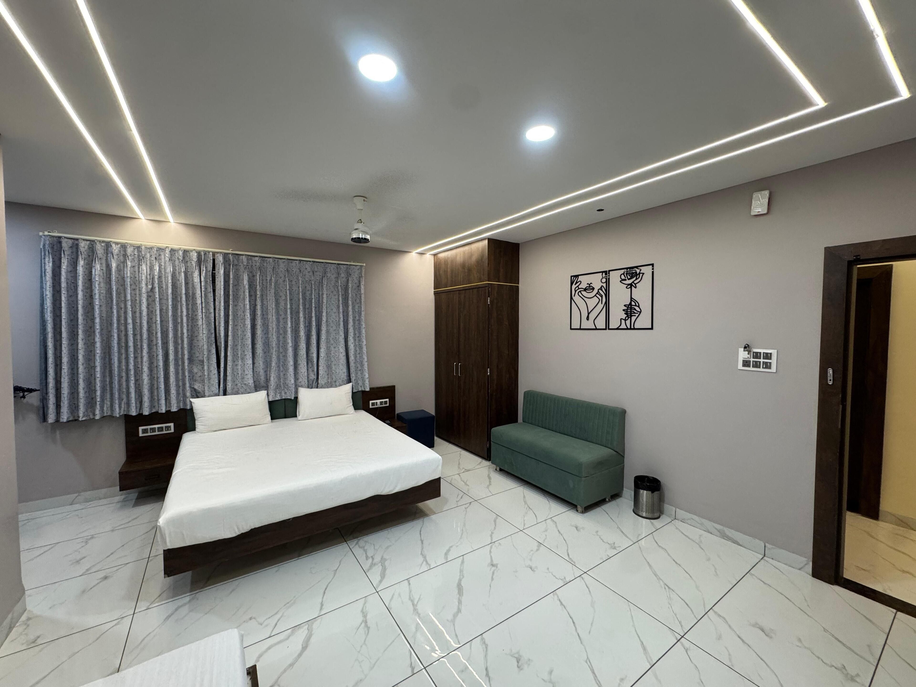 Quarto moderno com uma cama grande, um sofá verde, um guarda-roupa e iluminação embutida no teto.