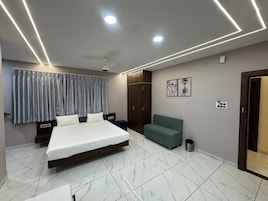 Quarto moderno com uma cama grande, um sofá verde, um guarda-roupa e iluminação embutida no teto.