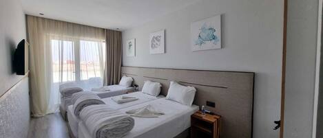 Quarto de hotel com duas camas, televisão, obras de arte na parede e piso de madeira.