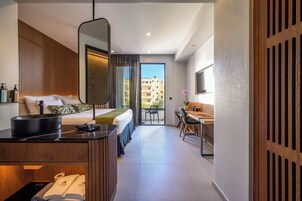 Quarto de hotel moderno com cama, escrivaninha e cadeira, um espelho grande e vista para a cidade.