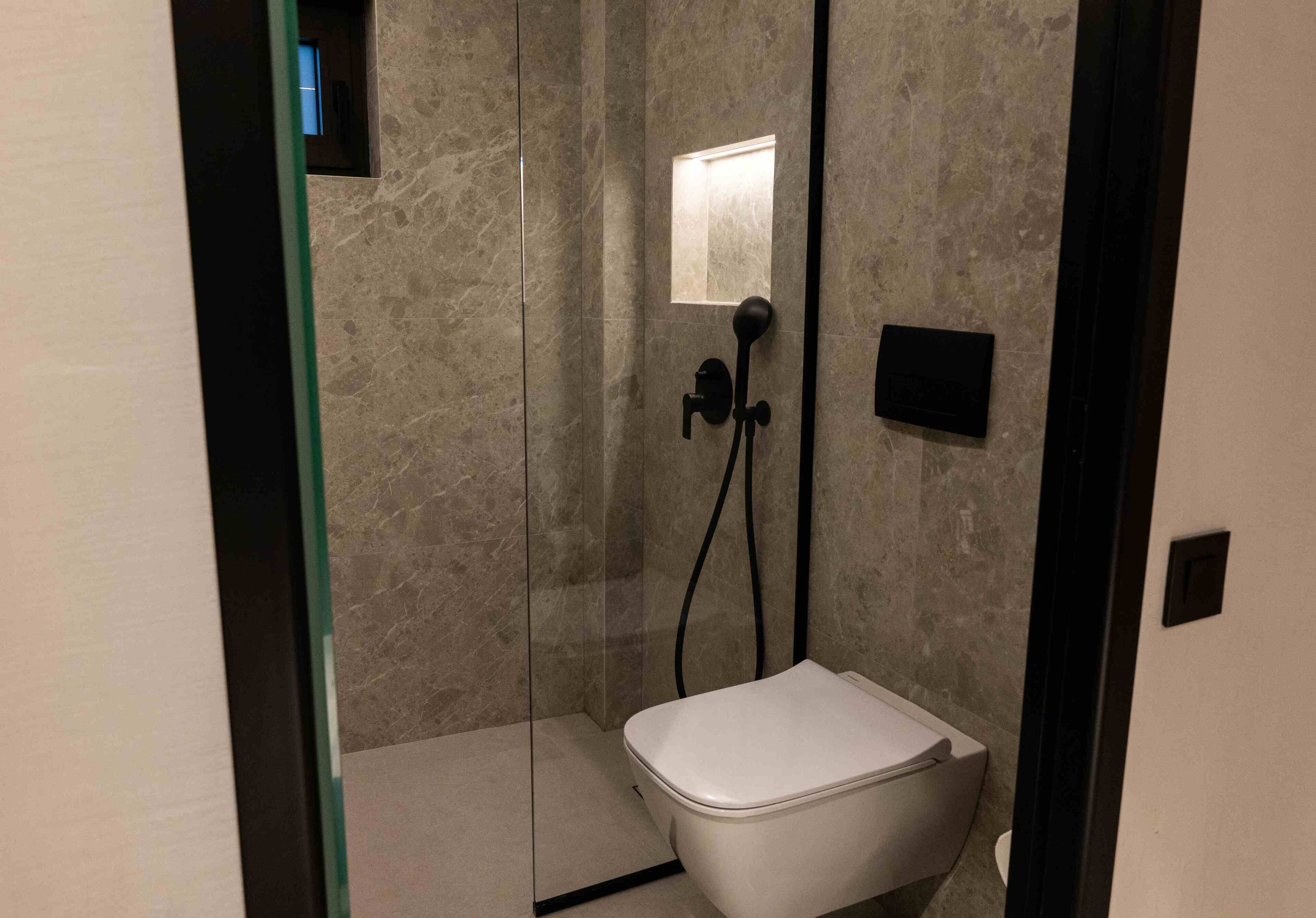 Um banheiro moderno com chuveiro em box de vidro, vaso sanitário branco e um pequeno painel iluminado na parede.
